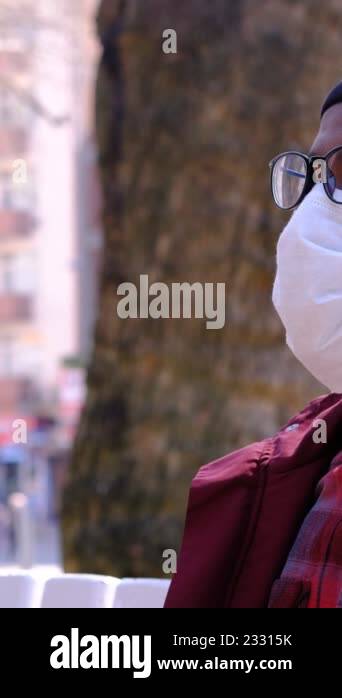 A young black man sitting on a bench taking off his mask face, masks ...