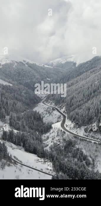 aerial view of highway passing through snowed forest on cloudy winter ...