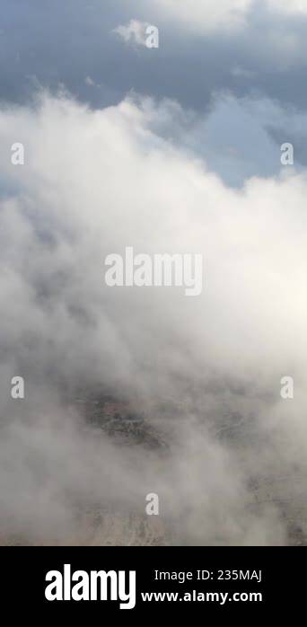 brown earthscape seen through white clouds, grey clouds on blue sky background above green land ...