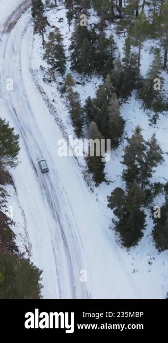 Drone view of vehicle driving on snow-covered forest road from far ...