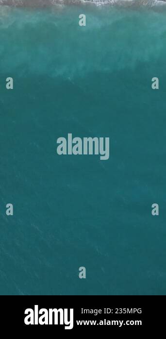 A drone view of the sea moving towards the shore and the waves crashing ...