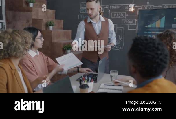 Team leader giving documents to group of employees talking to ...