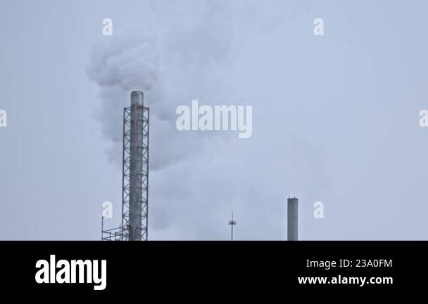 A tall smokestack is spewing smoke into the sky. The sky is overcast ...