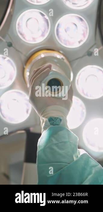 Vertical Screen: Gloved hand adjusting a surgical lamp in an operating ...