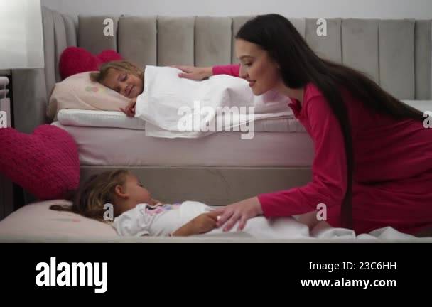 Mother lovingly tucks her two daughters into bed, creating a warm and ...