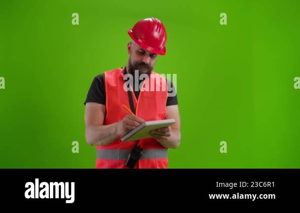 Construction worker in a red helmet and safety vest taking notes ...