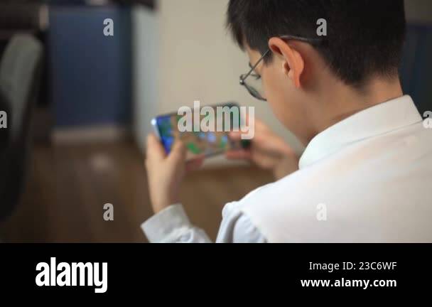 Close up of unrecognized young boy engaged in mobile game while sitting ...