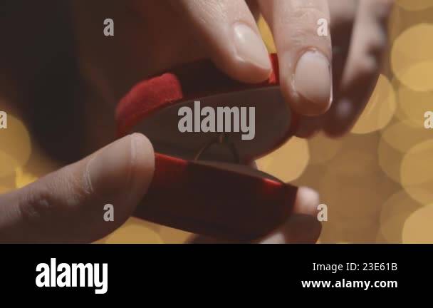 A closeup shows two hands holding a luxurious red velvet ring box with ...