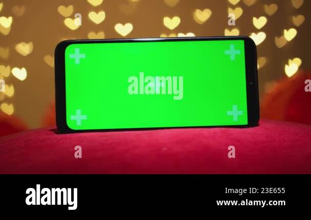 A modern smartphone with a vibrant green screen rests on a plush ...