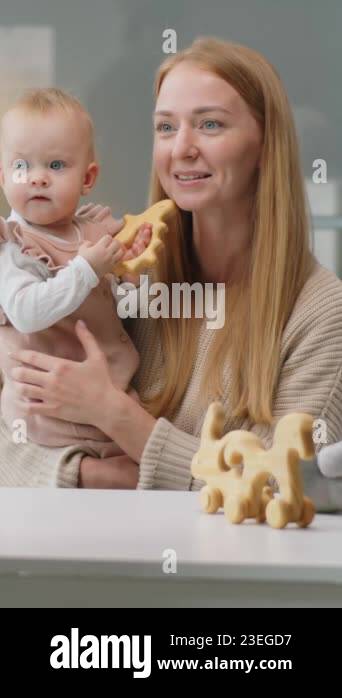 Vertical shot of young mother holding baby daughter on arms and talking to pediatrician while ...