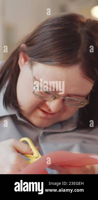 Vertical shot of young man with Down syndrome using scissors for ...