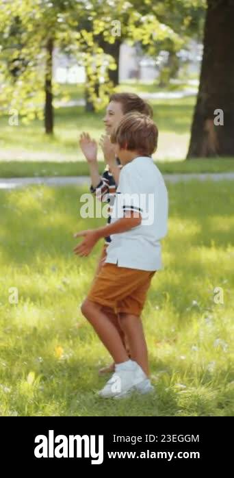 Vertical full shot of two excited boys clapping hands and dancing while ...