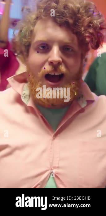 Vertical POV of tipsy guy with confetti on beard drinking alcohol from ...