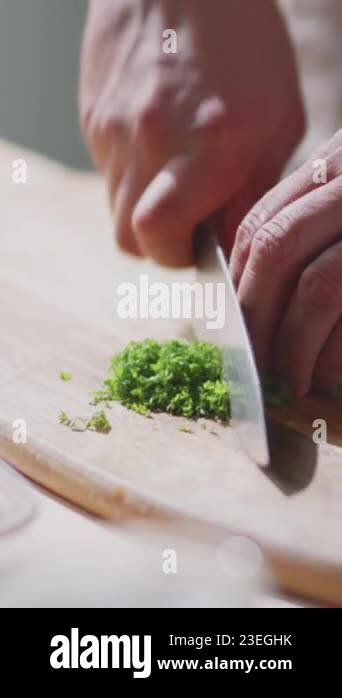 Vertical close-up shot of hands finely chopping fresh green herbs on ...