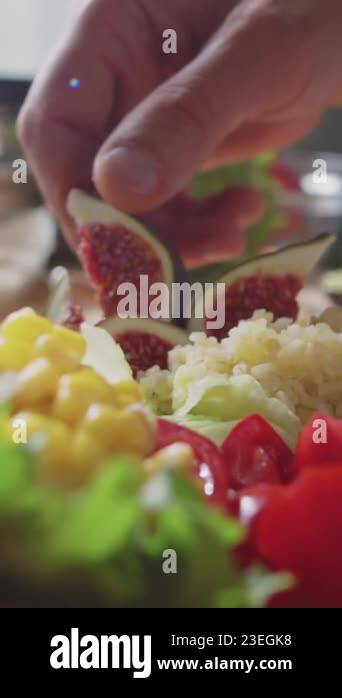 Vertical close-up shot of hand of male chef adding sliced fresh figs to ...