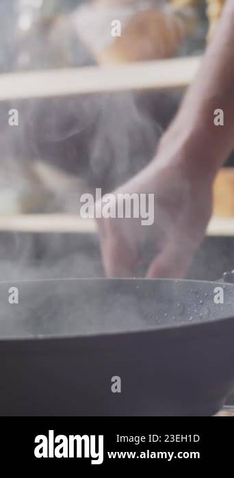 Vertical close-up shot of hand of chef pouring alcohol into frying pan ...