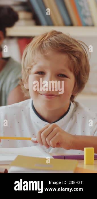 Vertical portrait shot of young school boy sitting at desk in classroom ...
