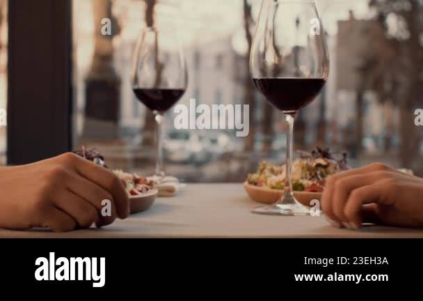 Two hands reach toward each other on a table, with wine glasses in the background, creating an ...