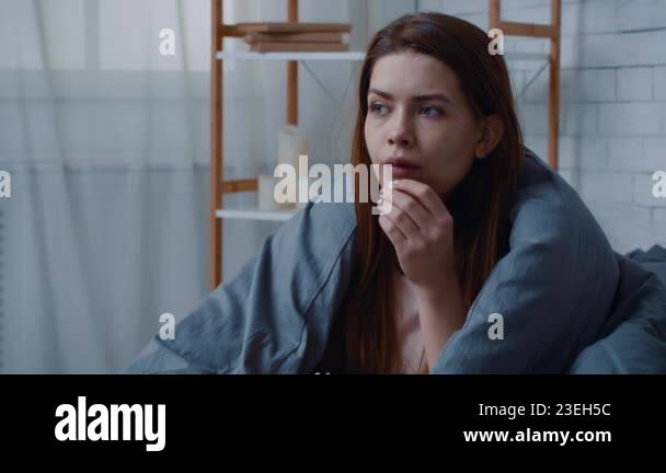 A millennial woman sits wrapped in a blanket, eating a snack, while ...