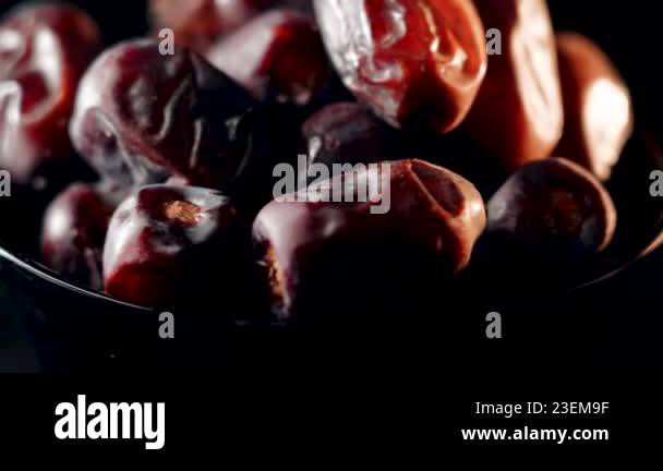 Dried dates rotate on a black background showcasing their rich texture ...