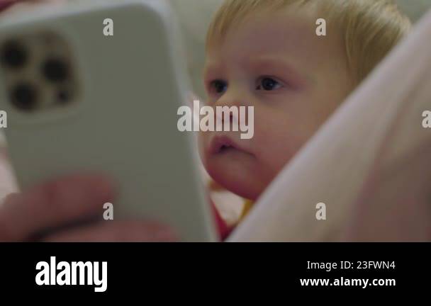 Curious toddler stares at smartphone screen, close up. Toddler ...