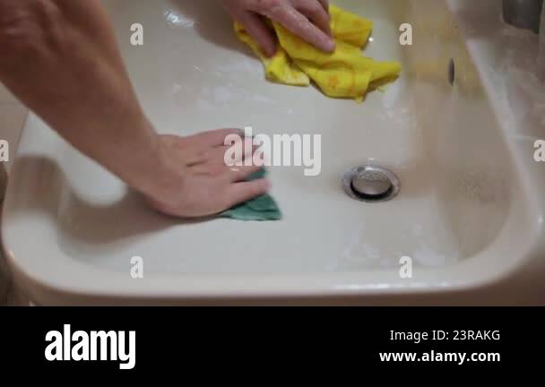 Cleaning bathroom wash basin with water and Glove holding yellow Sponge ...