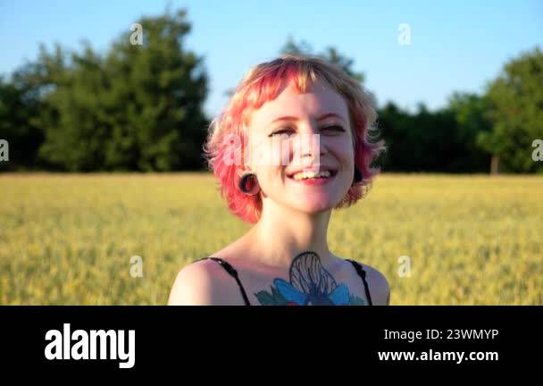 Portrait of happy punk girl with pink hair with blurred wheat field at ...