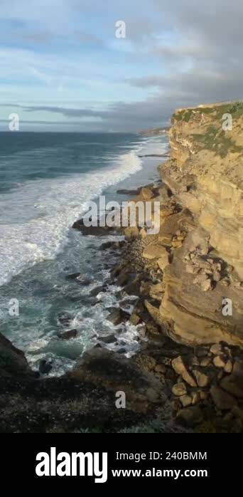 Vertical video of ocean waves crashing against a high rocky coastline ...