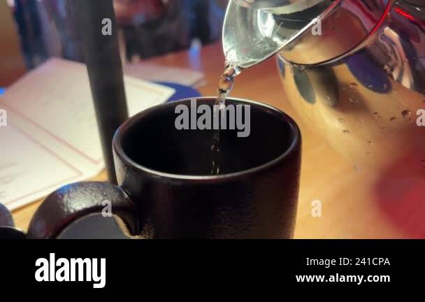 Pouring hot coffee into black coffee cup, mug with on old wood table in ...
