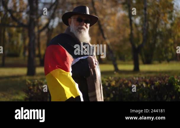 A senior German farmer standing confidently outdoors, draped in the ...