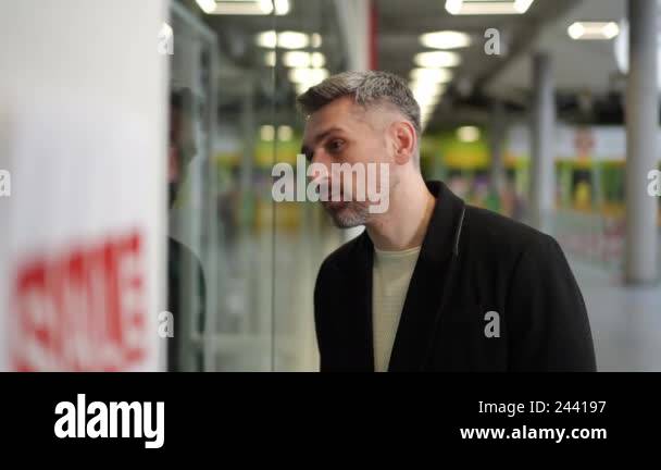 A man observes a storefront display, his reflection visible in the ...