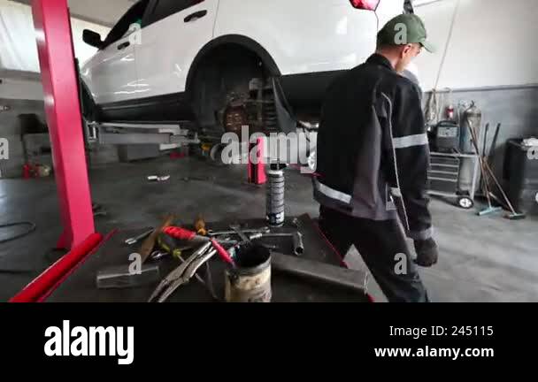 A mechanic walks under a car that is lifted up on a hydraulic lift to ...