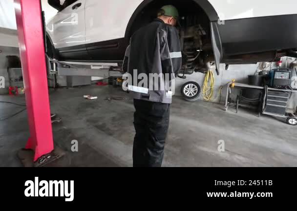 A car mechanic in a uniform is shown inspecting the undercarriage of a ...
