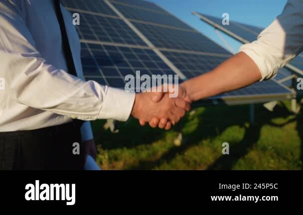 Close-up of two professionals shaking hands in front of solar panels ...