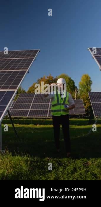 An engineer in a hard hat and safety vest reviews project plans while observing a large solar ...