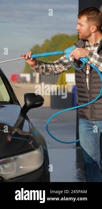 A man cleaning his car with a blue high-pressure hose, removing soap ...