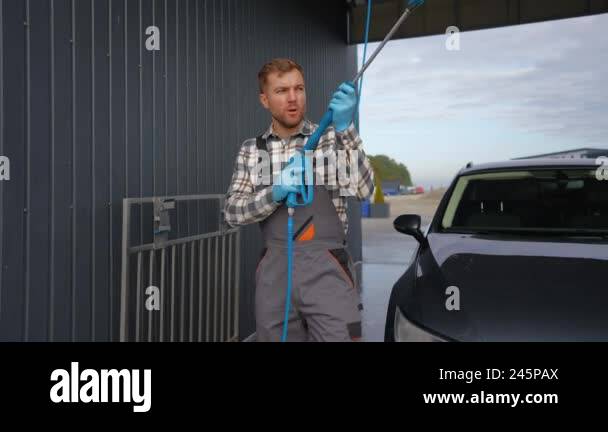 A playful car wash worker in gloves and uniform mimics shooting with a ...