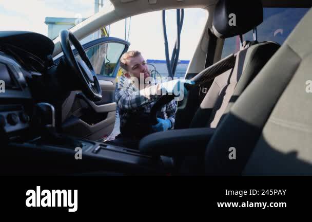 A professional car wash worker meticulously vacuums the interior of a ...