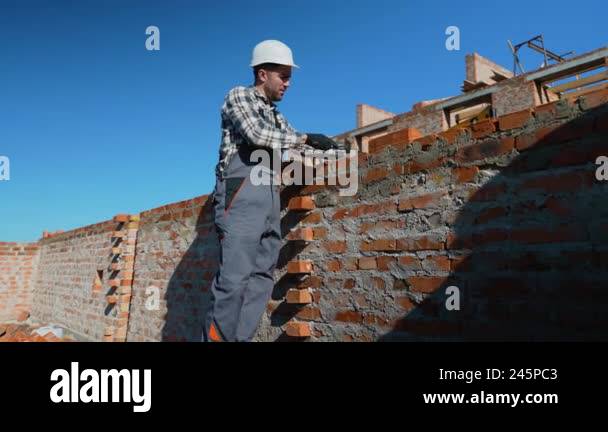 A construction worker in safety gear carefully lays bricks, building a ...