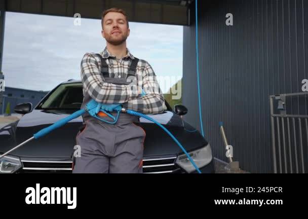 A professional car wash worker stands confidently with arms crossed ...
