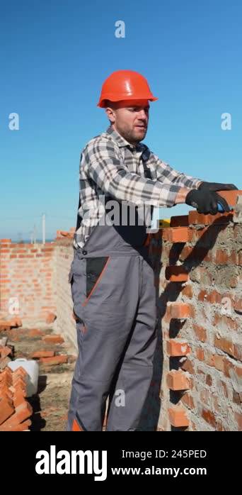 A skilled bricklayer wearing safety gear applies mortar to bricks while ...