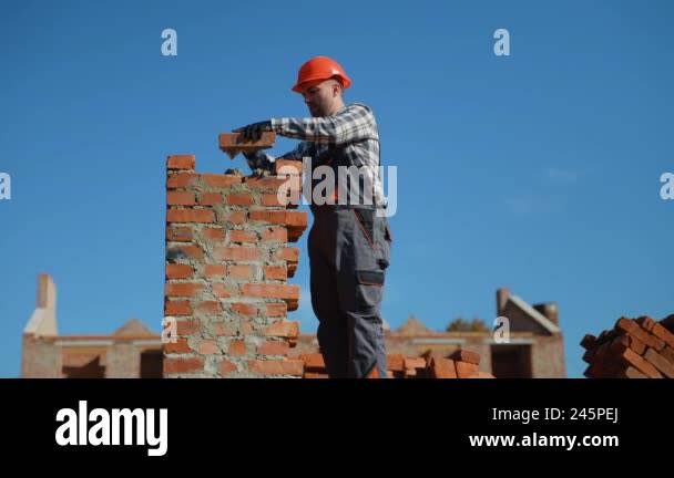 A construction worker in safety gear places bricks with precision while ...