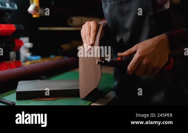 A craftsman uses a rotary tool to polish leather edges, achieving a ...