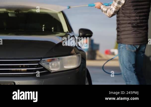 A close-up of a car being rinsed with a high-pressure water hose ...
