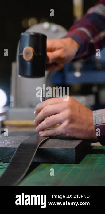 A focused leatherworker creating a belt in a workshop filled with tools ...