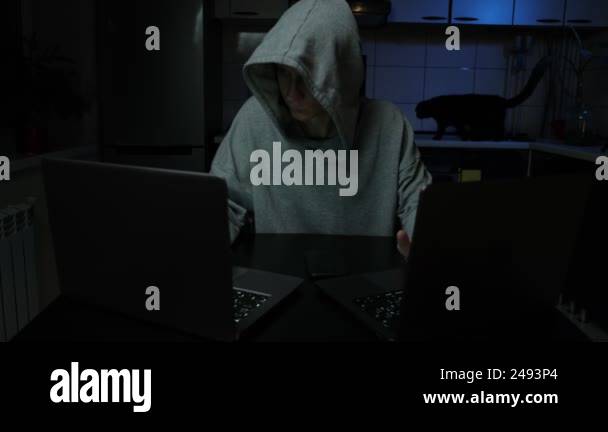 A hacker in a dark home office types rapidly on his laptop, symbolizing ...