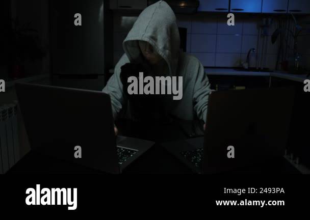 A hacker in a dark home office types rapidly on his laptop, symbolizing ...