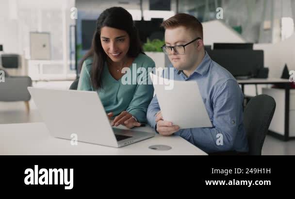 Young woman training man with Down syndrome sit at desk using laptop ...