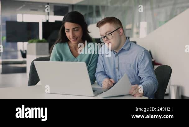 Man with Down syndrome and colleague sit at desk, collaborating on ...