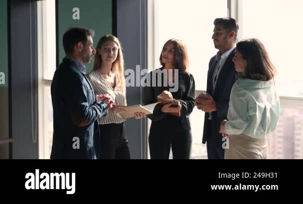 Diverse group of colleagues standing in circle, talking in office hall ...